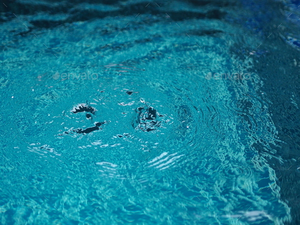 Rain drops falling blue water in pool background ripples surface texture, glittering bokeh ...